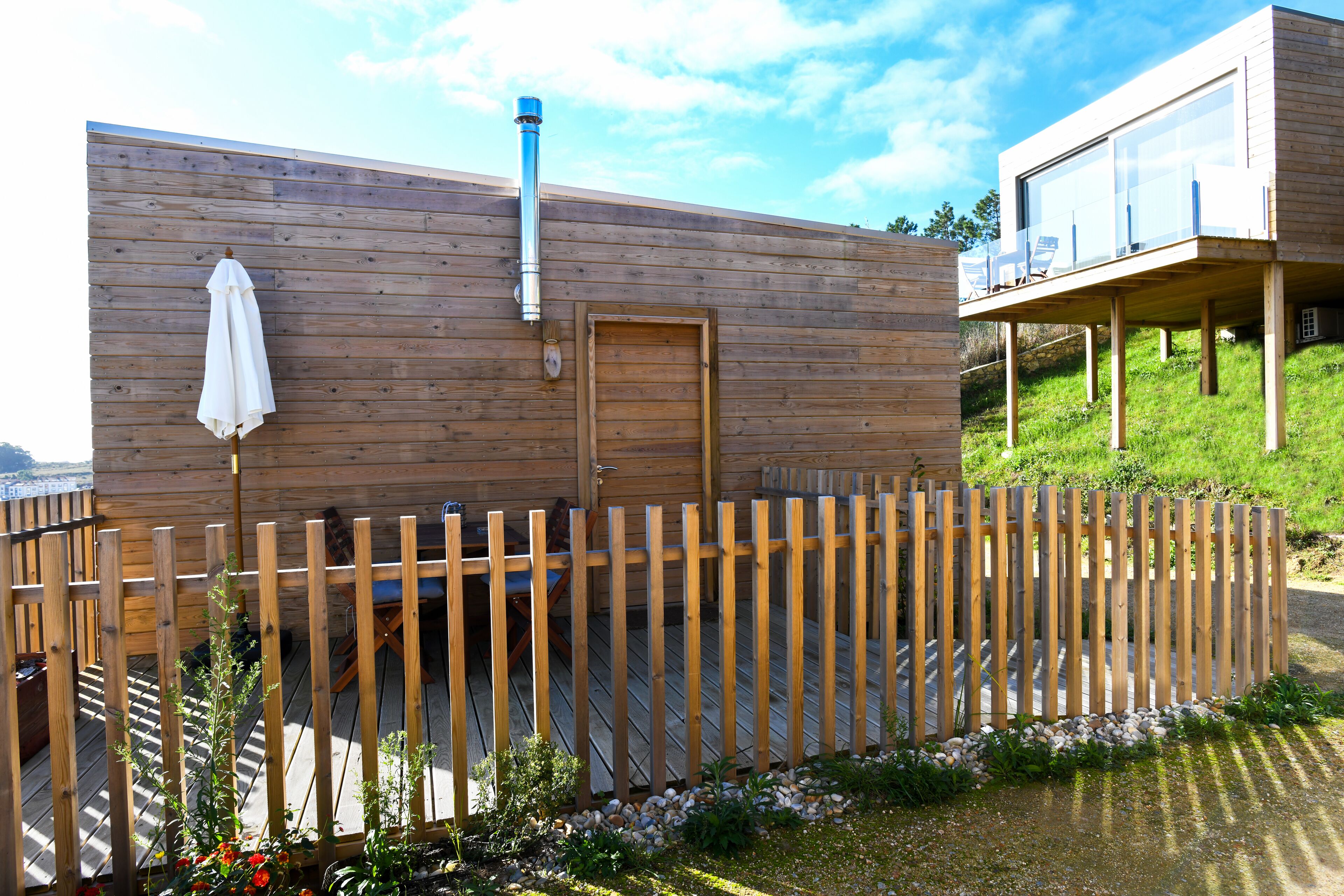 Uma cabana de madeira com varanda, porta e uma pequena área de estar ao ar livre.