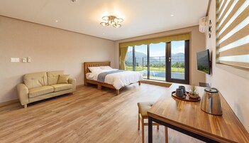 Quarto com cama, sofá, escrivaninha com chaleira e televisão.