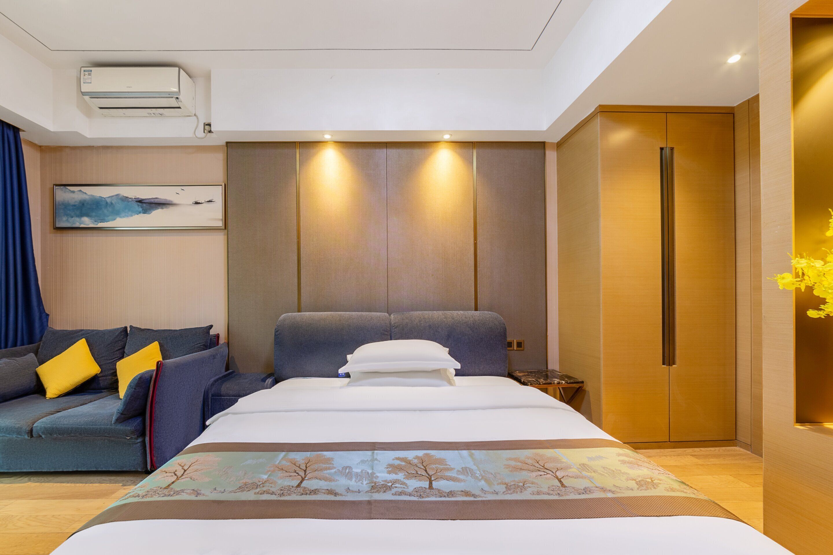 Quarto de hotel moderno com cama, sofá, ar condicionado fixado na parede e um quadro.