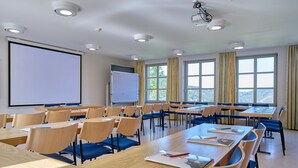 Uma sala de aula com carteiras de madeira, cadeiras azuis, uma lousa e uma tela de projetor.
