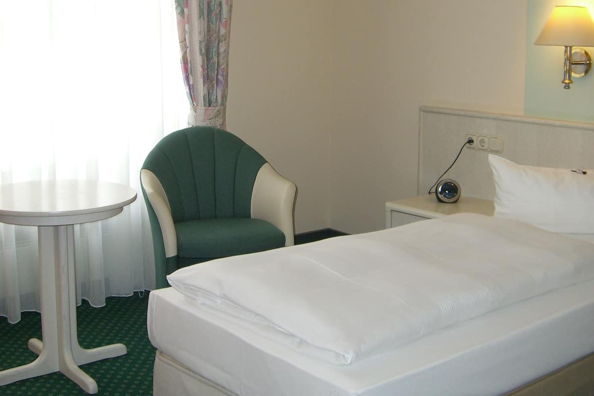Quarto de hotel com cama, cadeira, mesa e abajur.