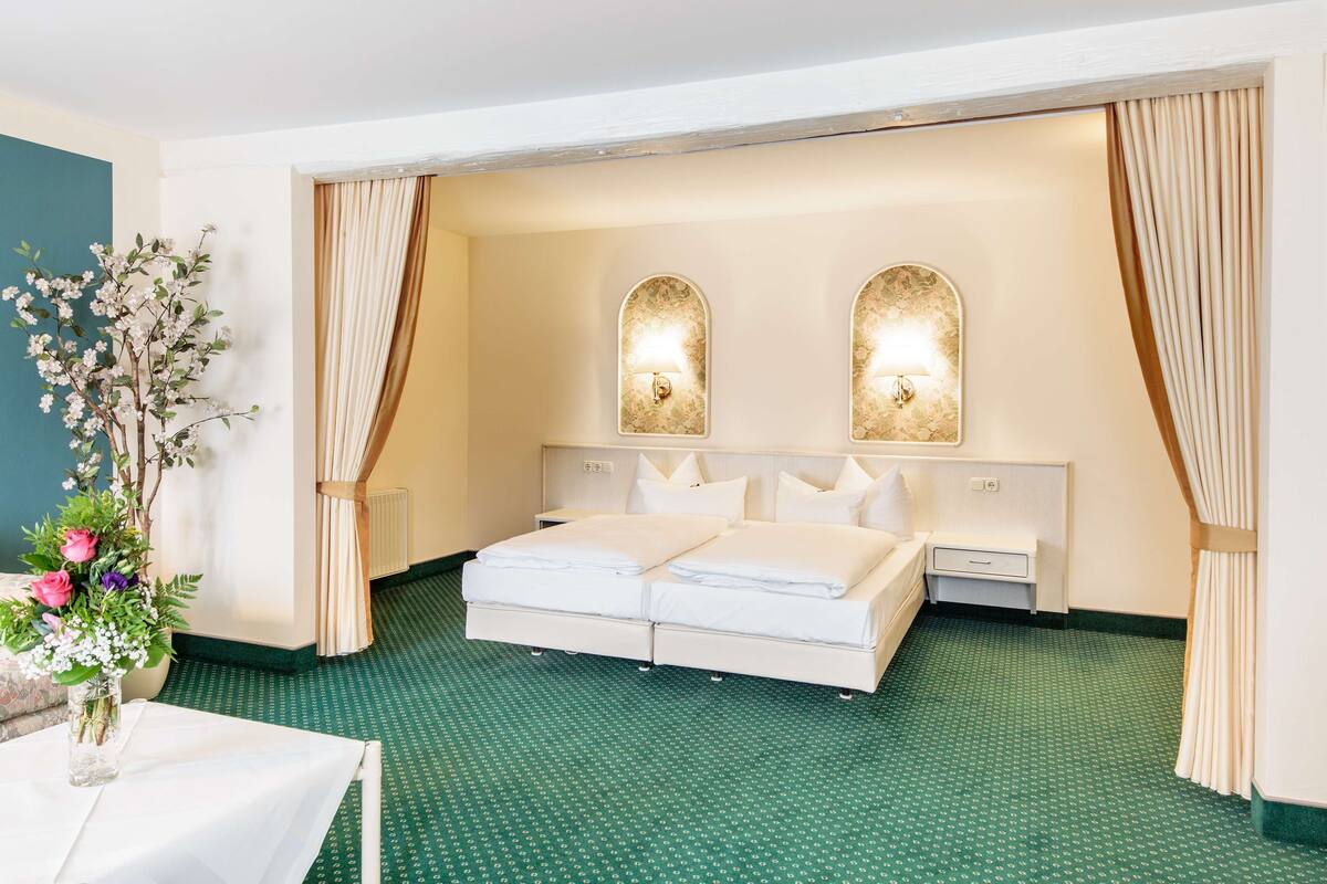 Quarto de hotel com cama de casal, mesa de cabeceira, espelho e um vaso com flores.
