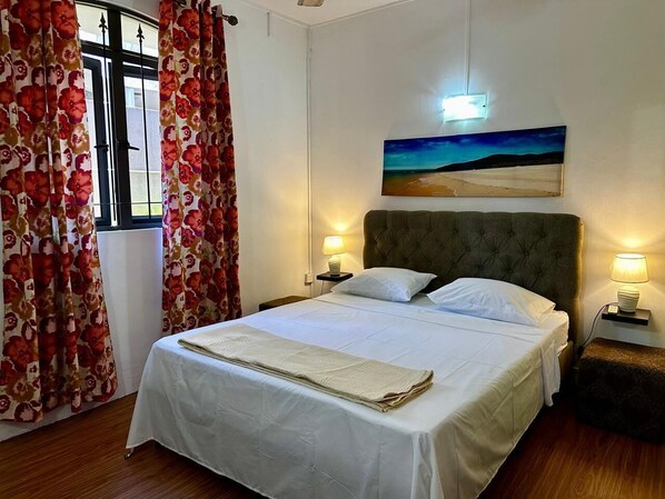 Cama bem arrumada com lençóis brancos, cabeceira e duas luminárias laterais.