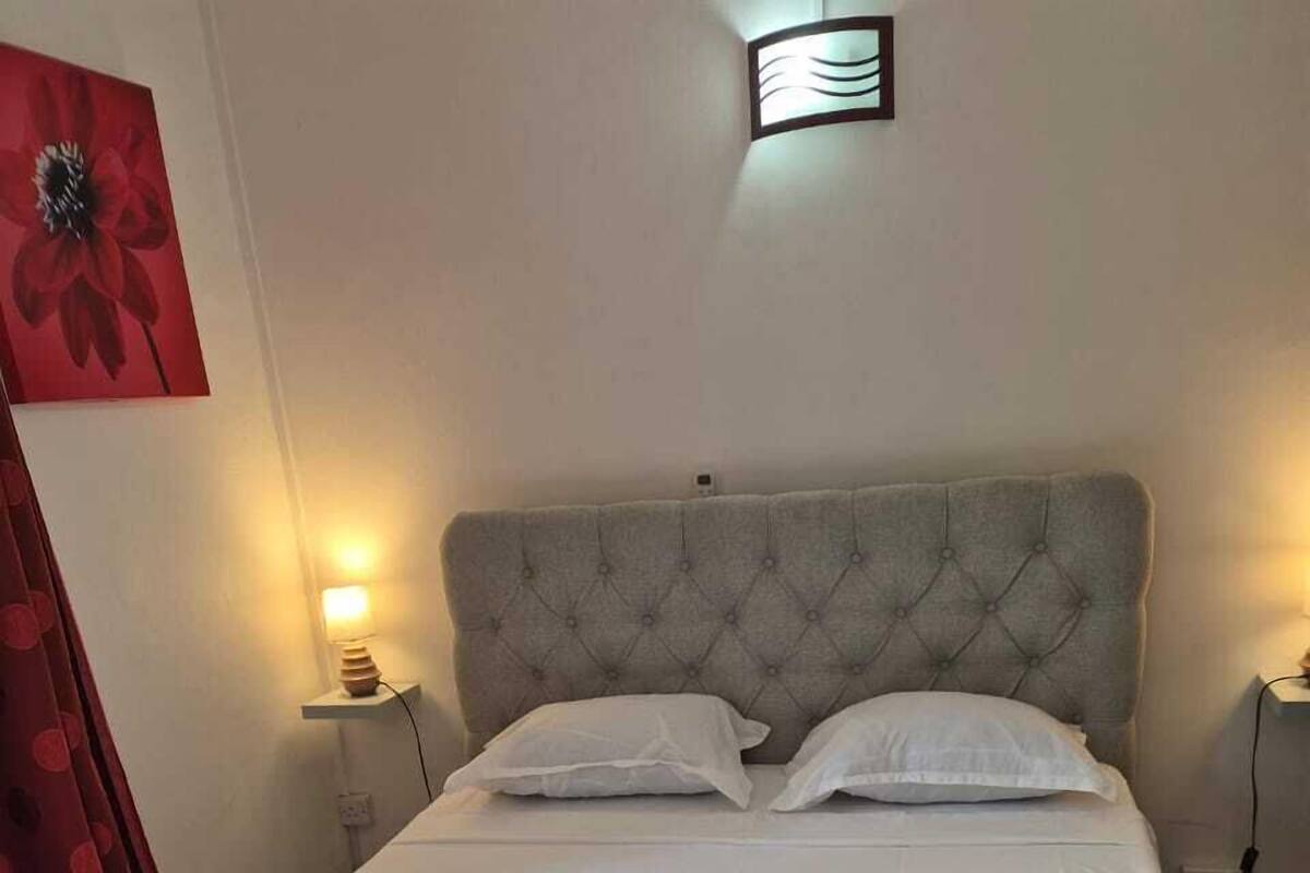 Uma cama bem arrumada com cabeceira estofada, roupa de cama branca e duas luminárias de cabeceira.