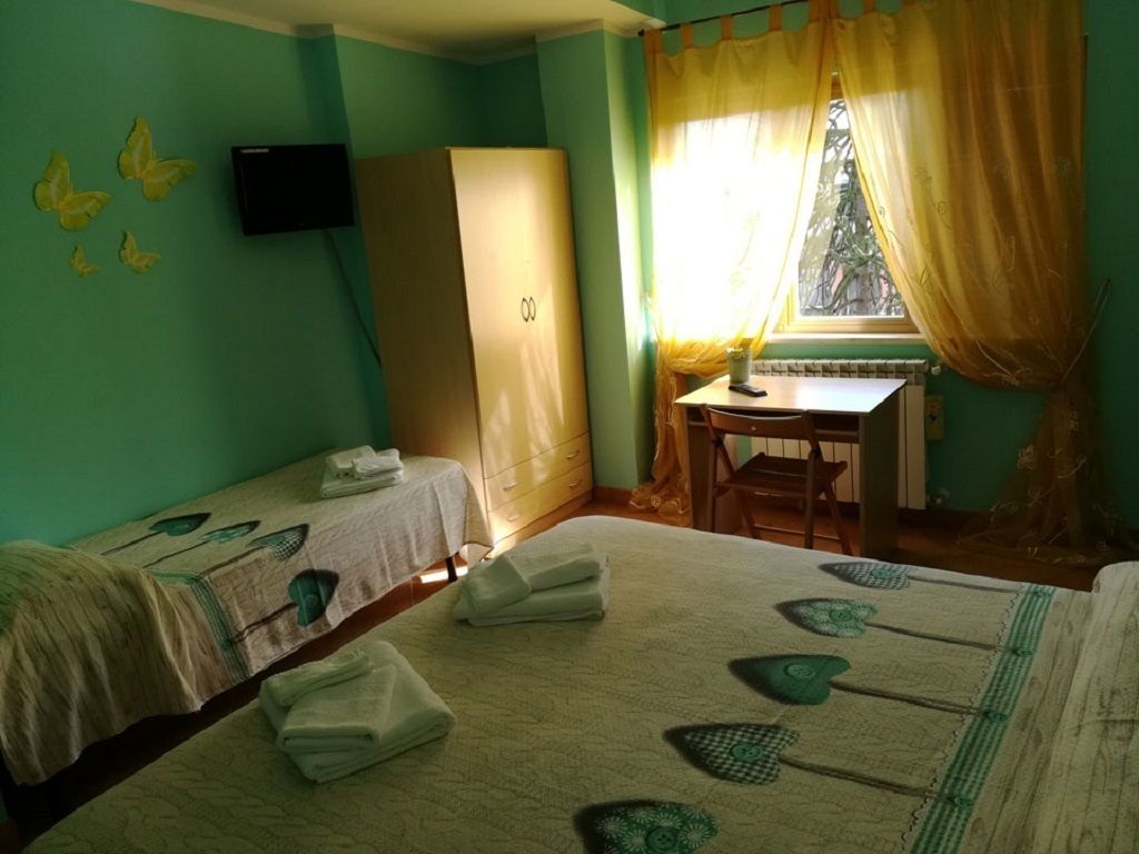 Quarto com duas camas, uma escrivaninha, um guarda-roupa e uma janela com cortinas.