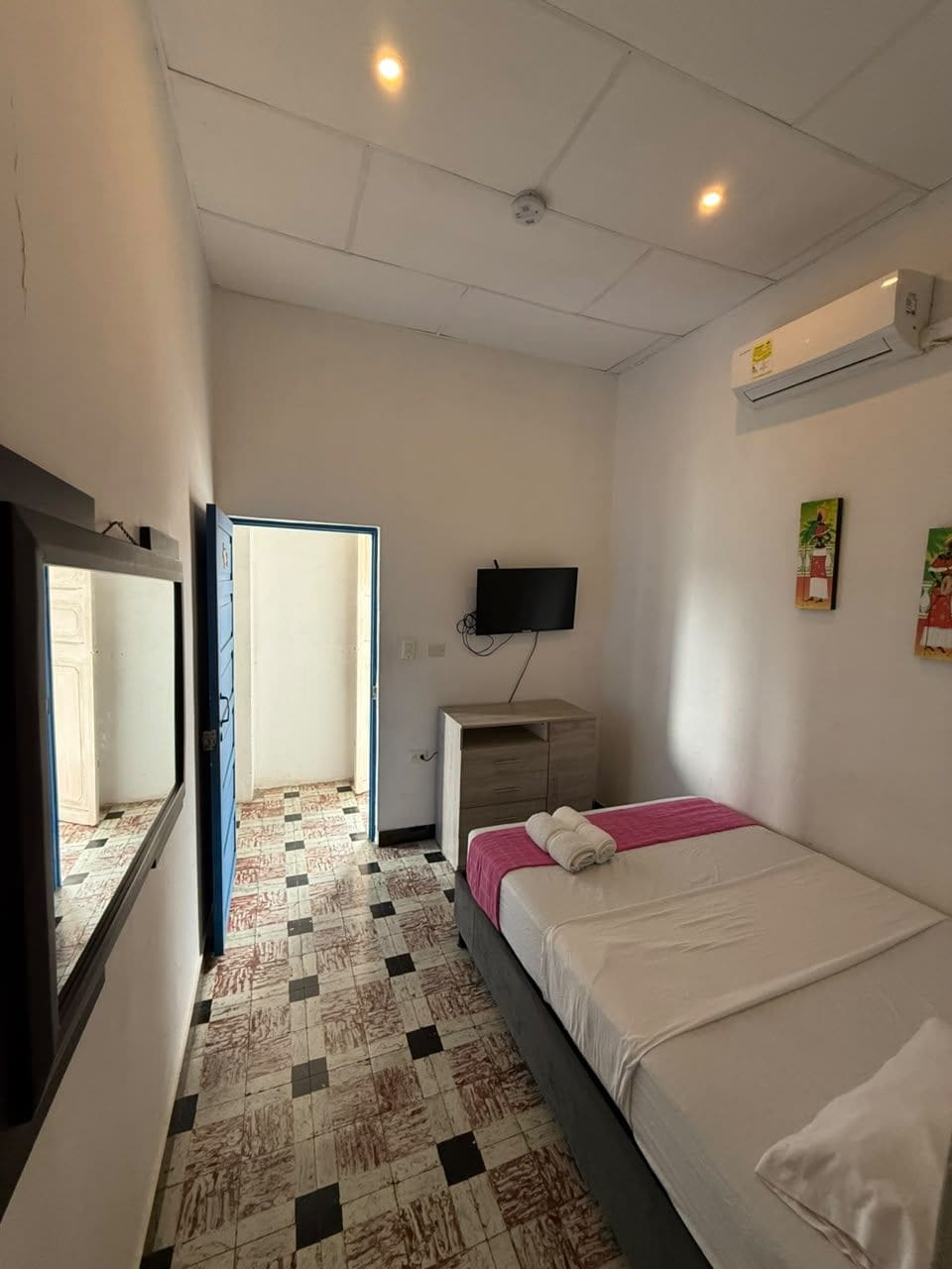 Quarto de hotel com cama, televisão, escrivaninha e piso estampado.