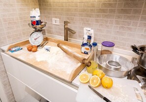 Uma bancada de cozinha com um rolo de massa, um medidor, ovos, limões e diversos utensílios de cozinha.