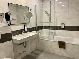 Um banheiro moderno com um espelho grande, uma pia, uma banheira e um chuveiro.