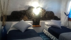 Quarto com duas camas, parede de pedra e janela com persianas.