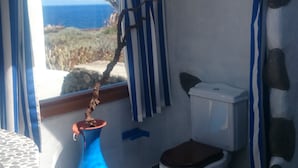 Casa de banho com sanita, um vaso azul e vista para o mar.
