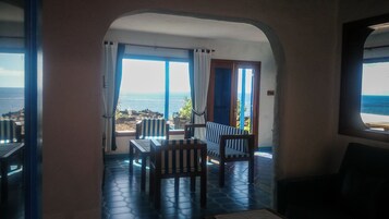 Quarto com vista para o mar, com mesa e cadeiras, janela com cortinas e piso de azulejos.