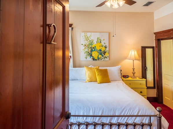 Quarto com cama, mesa de cabeceira, luminária, quadro e porta de madeira.