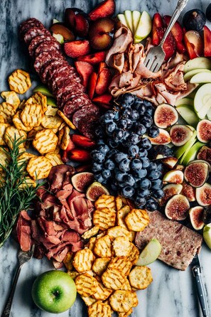 Tábua de frios com diversos embutidos, queijos, frutas e biscoitos.