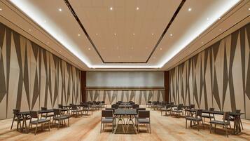 Sala de conferências com várias mesas e cadeiras, uma tela grande na frente e um design de parede estampado.