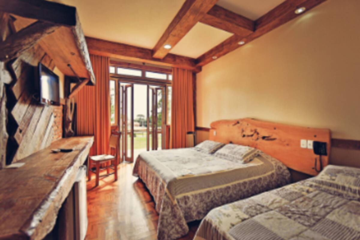 Quarto com duas camas, um banco de madeira, televisão e uma porta de vidro deslizante que dá para uma área externa.