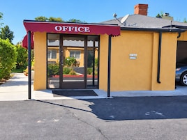 Um edifício com toldo vermelho com a placa 'OFFICE' e um aviso indicando local para entrega de chaves.