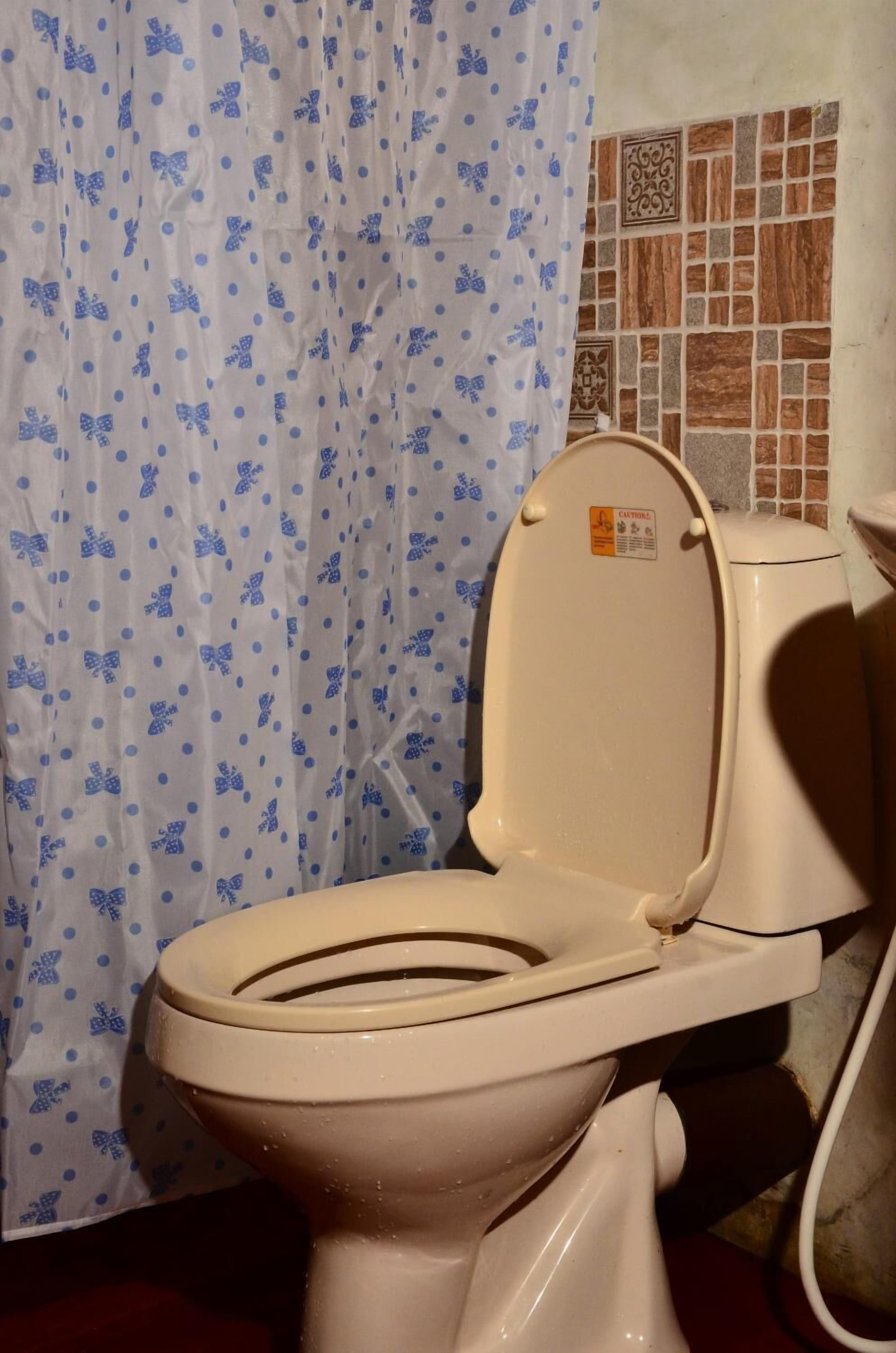 Sanitário com etiqueta de aviso, cortina de borboleta azul e parede revestida de azulejos.