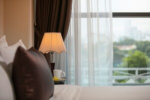 Quarto de hotel com uma cama, luminária, xícara e vista para a paisagem urbana através de grandes janelas.