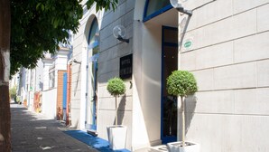 Fachada de hotel com porta azul, placa indicando ser um hotel e duas árvores em vasos na frente.