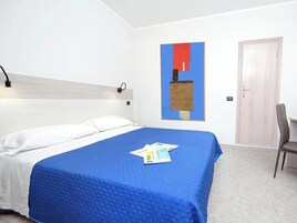 Quarto de hotel com uma cama, uma mesa, uma cadeira e uma porta.