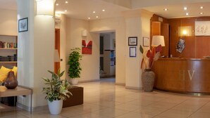 Um saguão de hotel com uma mesa de recepção, uma área de estar com um sofá e uma mesa de centro, uma estante de livros e uma televisão.
