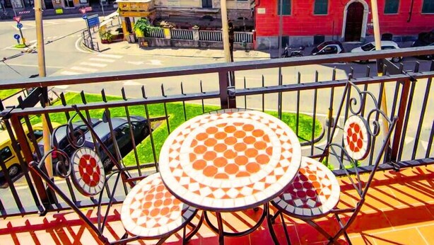 Uma varanda com mesas e cadeiras redondas, com vista para uma rua com edifícios coloridos.
