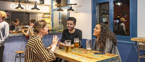 Um grupo de pessoas sentadas em uma mesa de madeira num bar com detalhes em azul e luminárias pendentes.