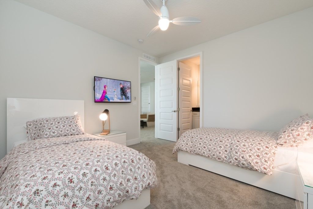 Quarto com duas camas, um ventilador de teto, uma televisão e uma porta que dá para outro cômodo.