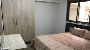 Quarto com cama, mesa de cabeceira, guarda-roupa de madeira e janela com persianas.