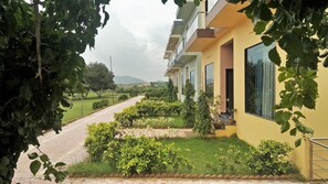 Um edifício moderno com fachada amarela, estrada pavimentada e vegetação bem cuidada.