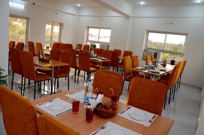 Uma sala de jantar com várias mesas e cadeiras laranja, janelas amplas com vista e um interior limpo e moderno.