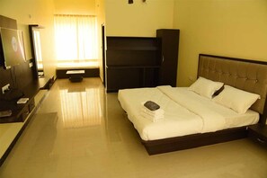 Quarto de hotel com cama, televisão, escrivaninha e janela com cortinas.