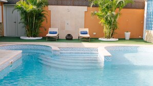 Piscina com duas cadeiras de descanso e plantas em vasos.