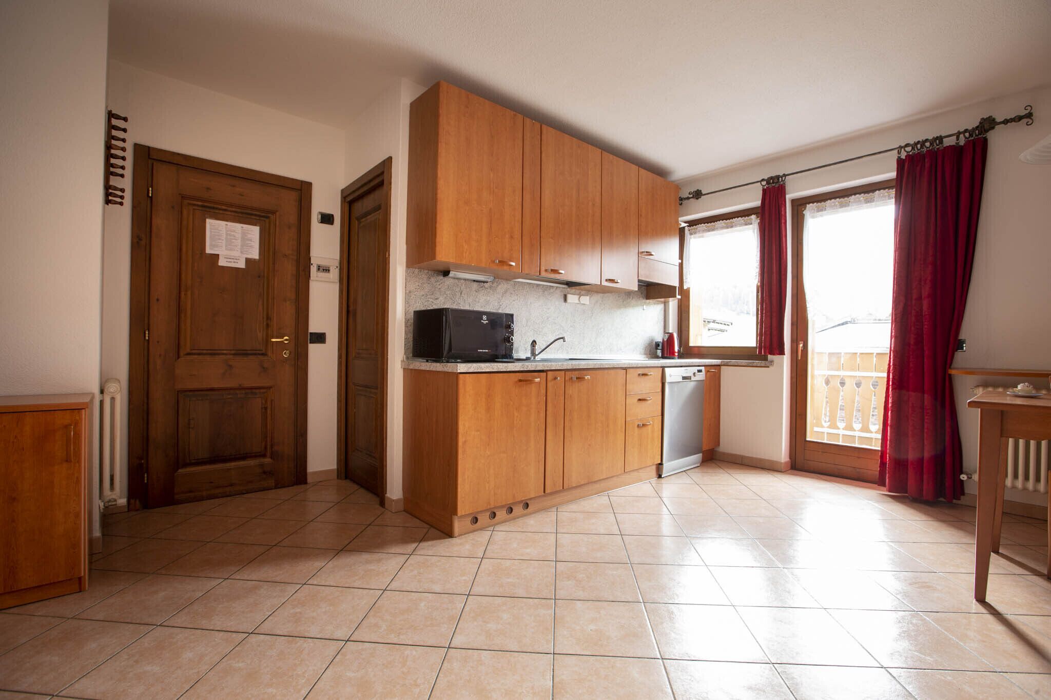 Cozinha com armários de madeira, geladeira preta e janela com cortinas vermelhas.