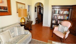 Uma sala de estar com sofá, poltrona, abajur, estante de livros e lareira.