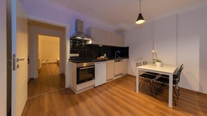 Cozinha moderna com área de jantar, piso de madeira, armários brancos e uma luminária pendente sobre a mesa.