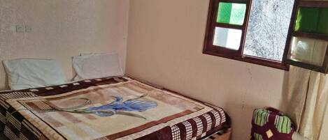 Quarto com cama, janela com vista para árvores e tapete estampado.
