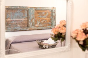 Quarto com espelho refletindo um painel de madeira rústica, uma cesta de vime com tecido branco e um vaso com flores.