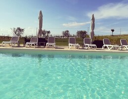 Piscina com água cristalina, rodeada por espreguiçadeiras e guarda-sóis brancos.