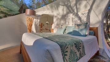 Quarto com cama, abajur e janela com vista para árvores.