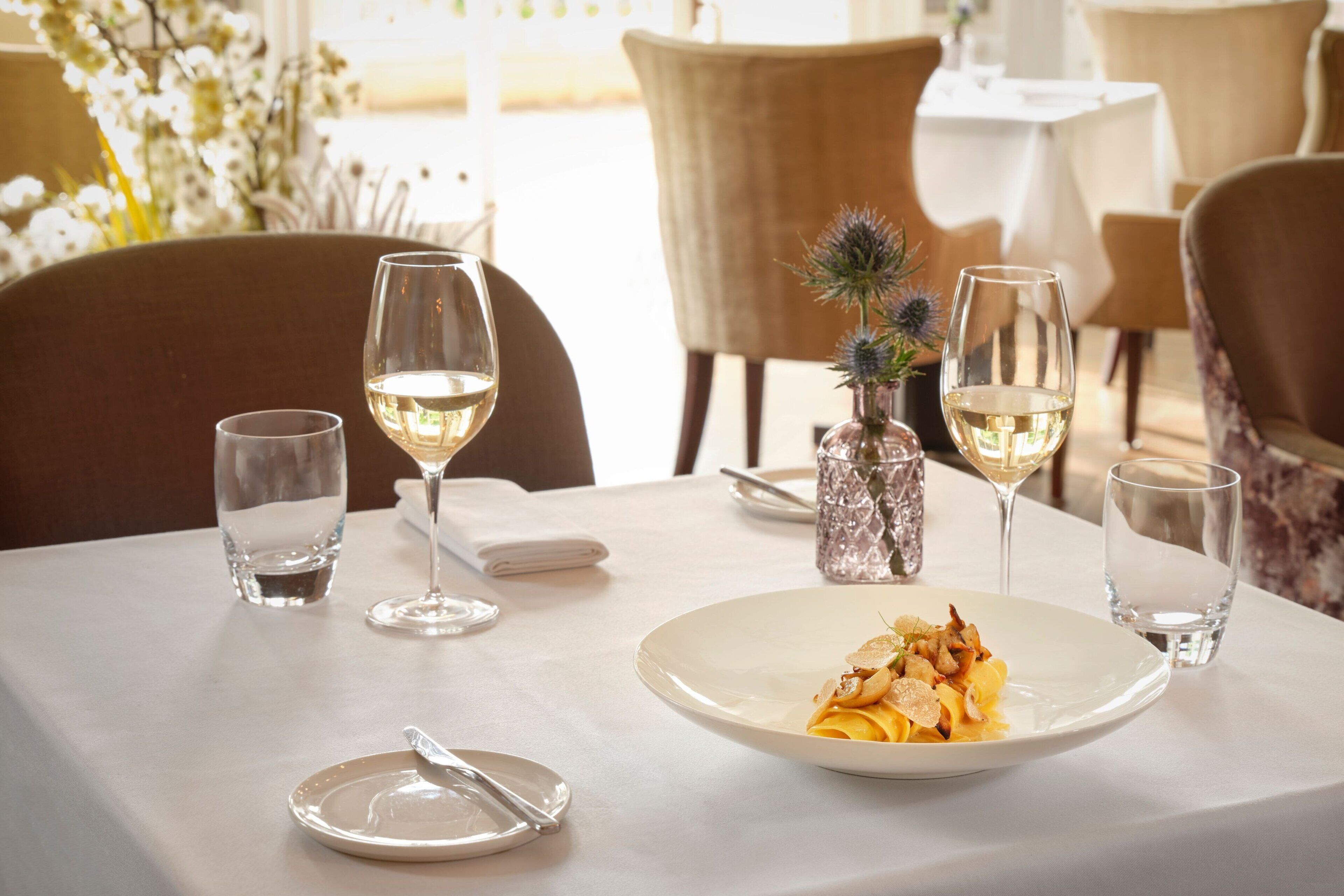 Uma mesa de jantar com um prato de comida, copos de vinho e talheres.