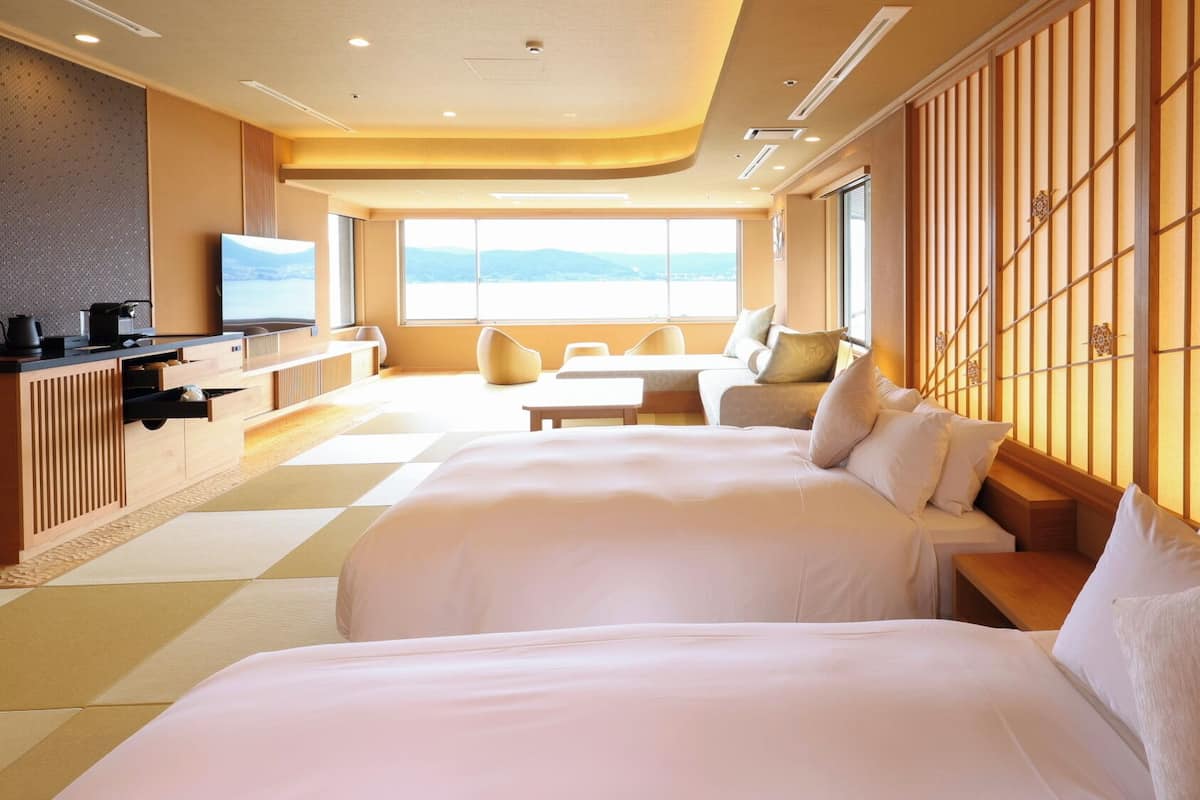Quarto de hotel com duas camas, televisão, escrivaninha e vista para as montanhas.