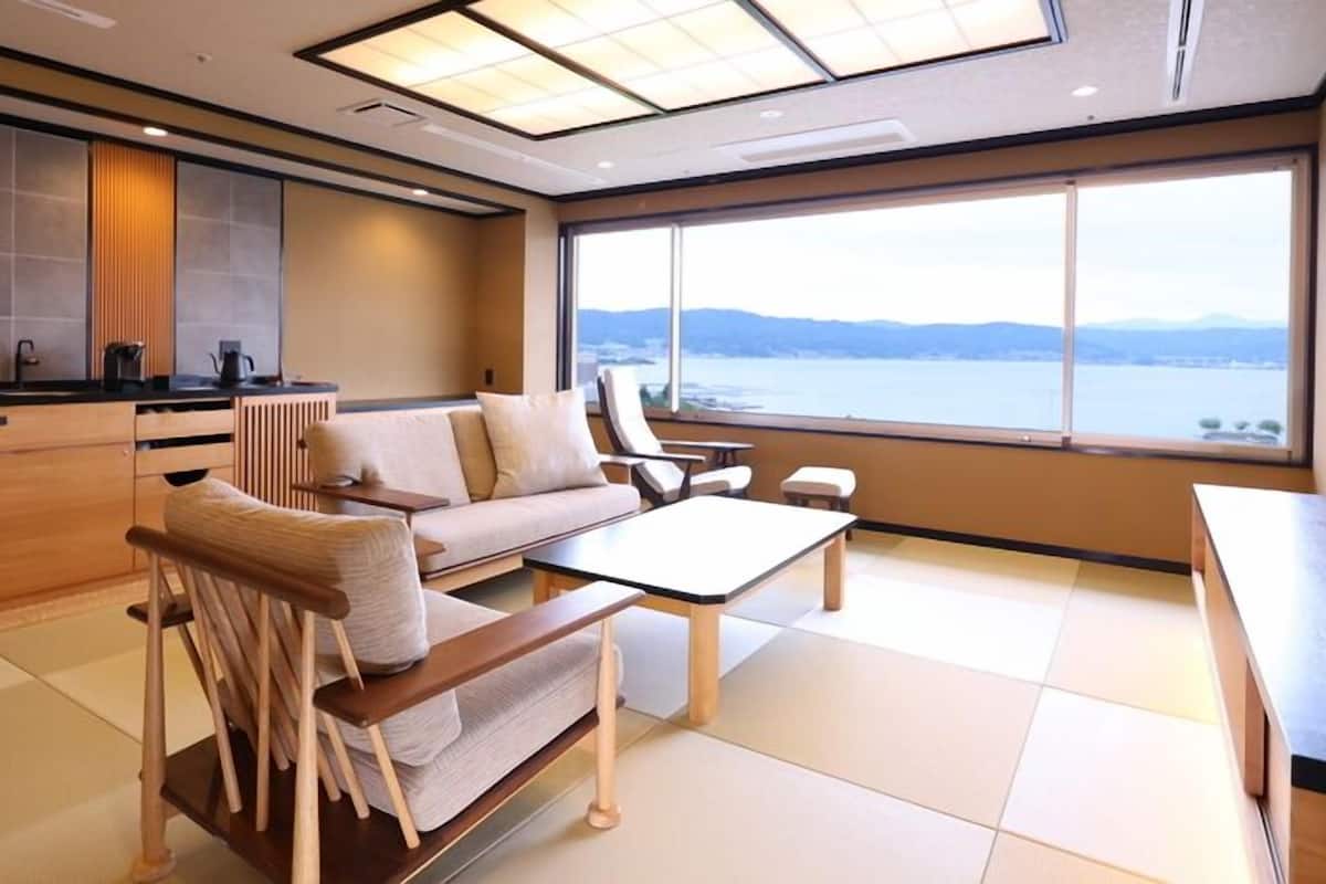 Um interior moderno com um sofá, cadeiras, uma mesa e vista para um corpo d'água.