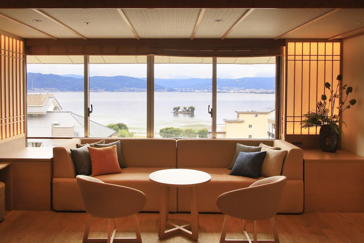 Quarto com sofá, duas cadeiras, uma mesinha e vista para um corpo d'água e edifícios ao longe.