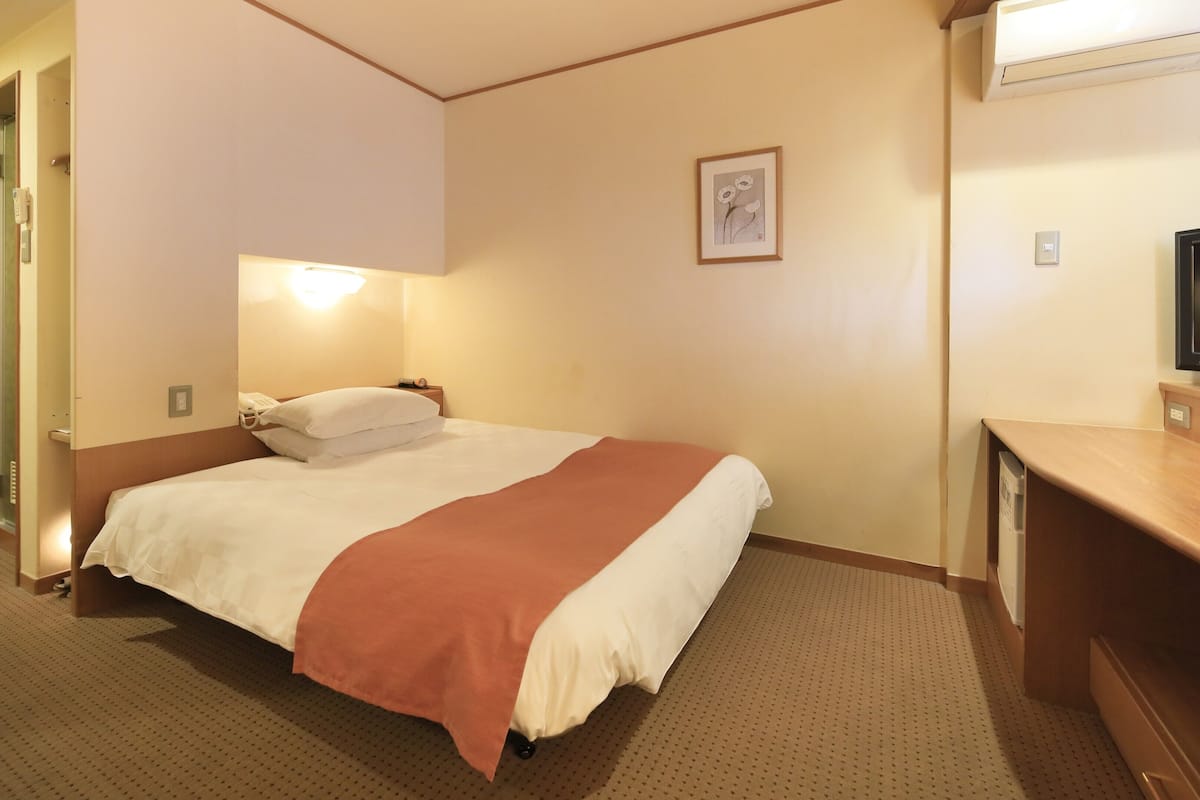 Quarto de hotel com cama, mesa de cabeceira, televisão e ar condicionado.