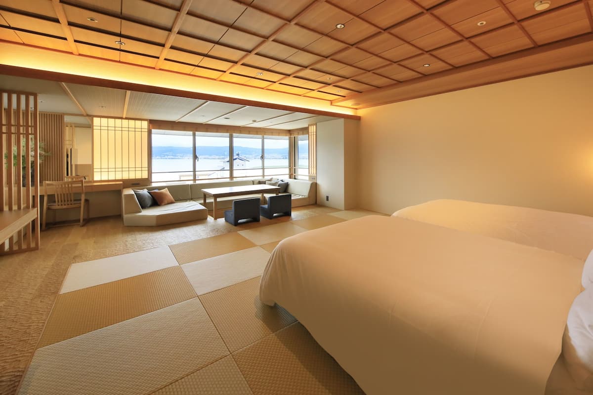 Quarto de hotel com uma cama grande, um sofá, uma mesa de jantar e vista para o mar.