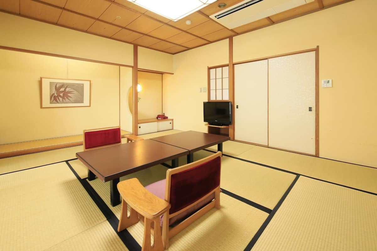 Um quarto japonês tradicional com tatames, uma mesa baixa e uma televisão.