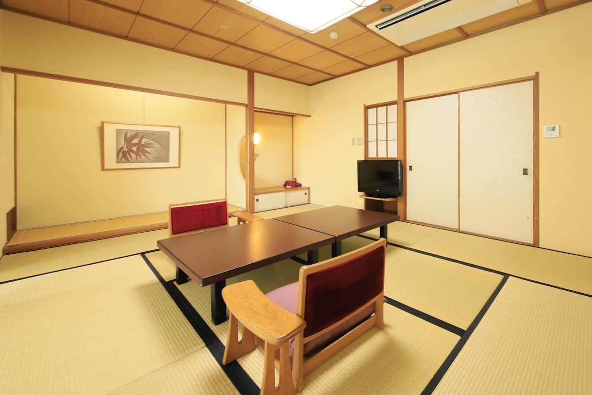 Um quarto japonês tradicional com tatames, uma mesa baixa e uma televisão.