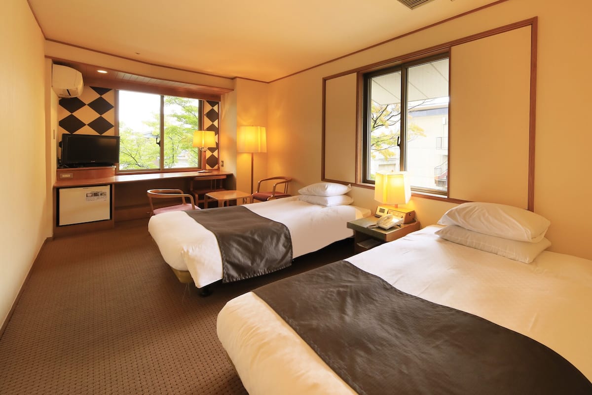 Quarto de hotel com duas camas, uma escrivaninha com um computador, uma cadeira e uma janela com vista.