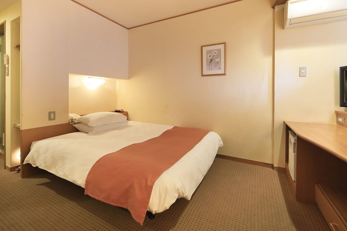 Quarto de hotel com cama, abajur, televisão e um quadro na parede.